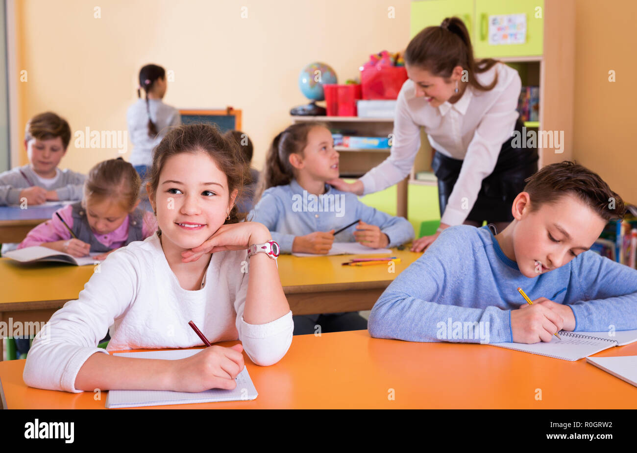 Portrait of young pleasant teacher woman at lesson with diligent school ...