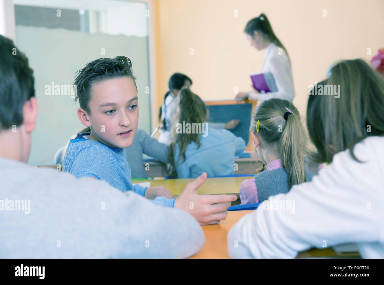 Happy pupils chattering sitting on back desks at lesson in elementary ...