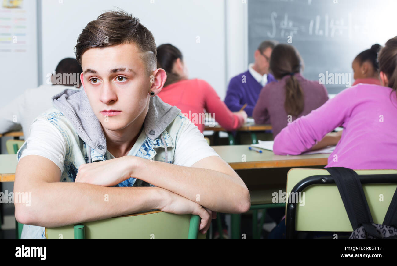 Portrait of a sad outcast student sitting lonely while others listening ...