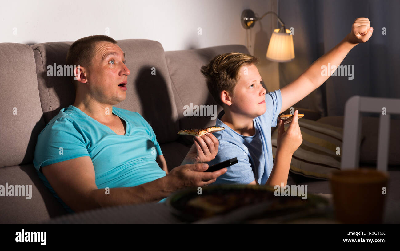 Man and his son are happy because their football team is wining at home ...