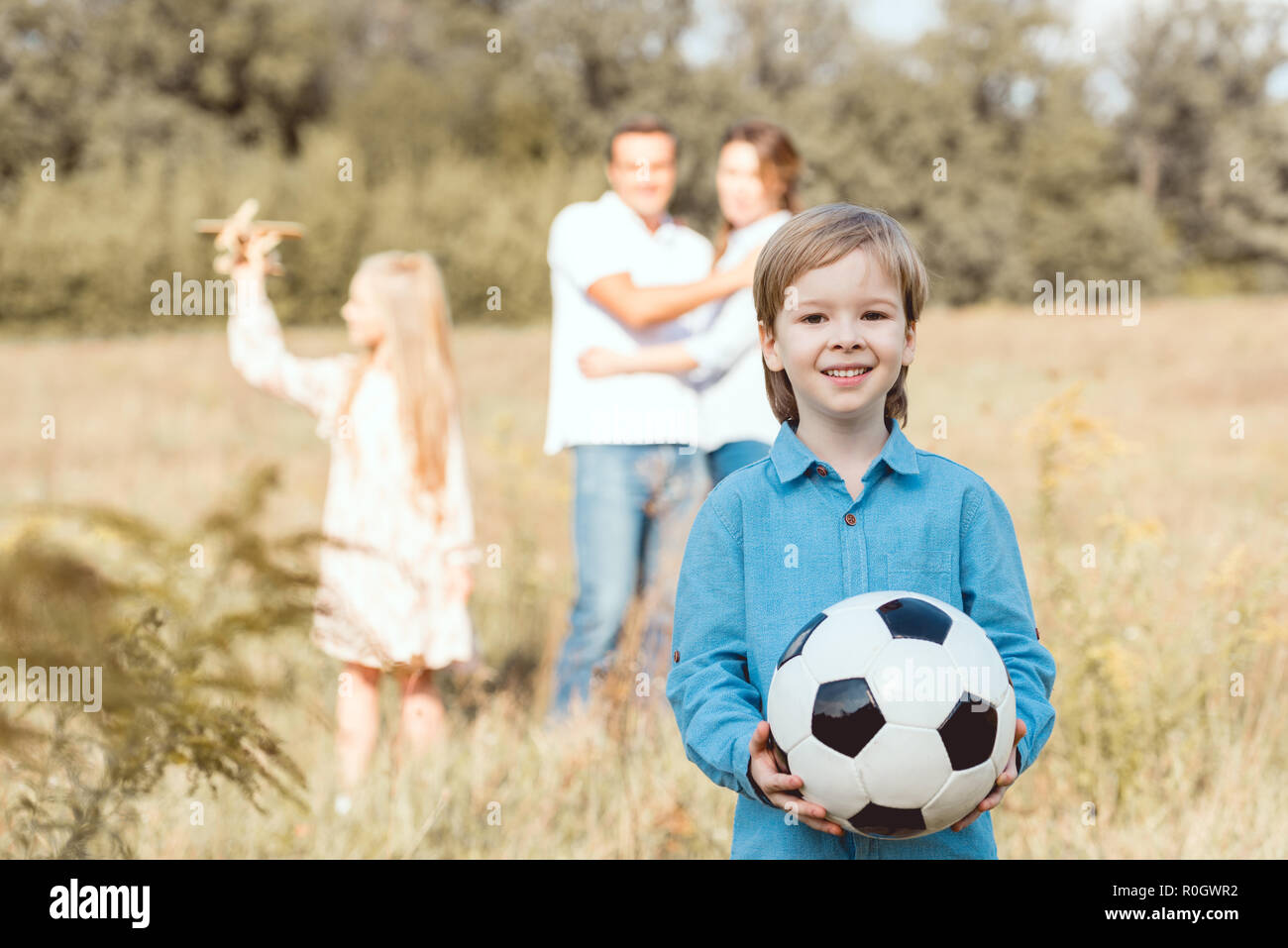 adorable little kid holding ball while his family standing blurred on ...