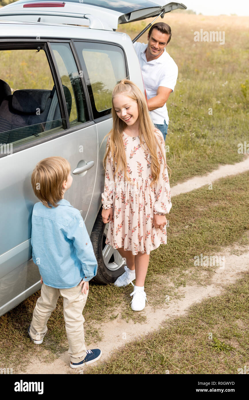 adorable little kids standing near car while their father opening trunk ...