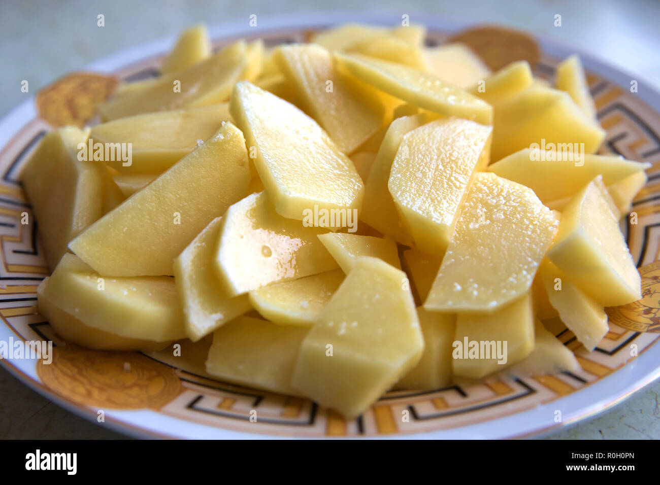 Uncooked cubical yellow potatoes on a chopping board. In the chopped ...