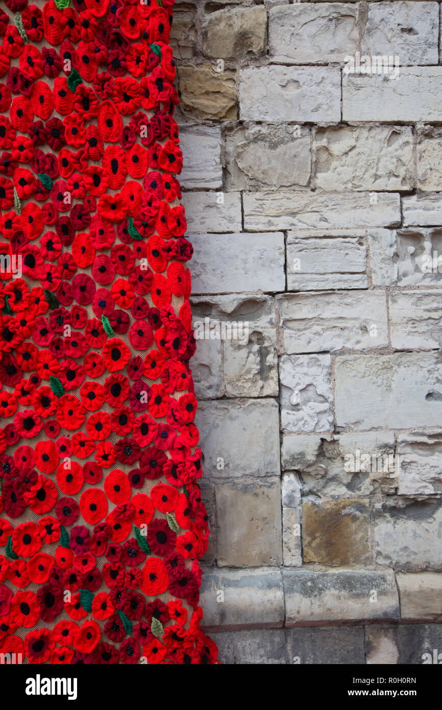 Handmade knitted and crocheted poppies decorating the stone wall of a ...