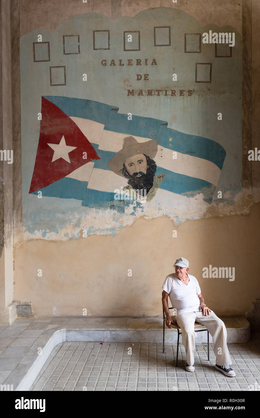 Man sitting in front of tribute to heroes of the Cuban revolution ...