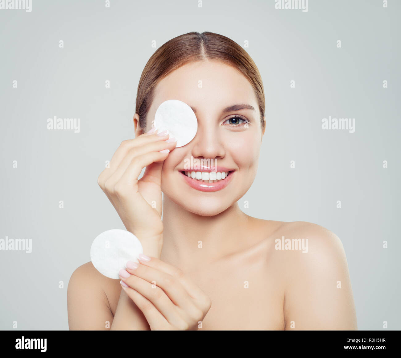 Cheerful woman removing face makeup with a cotton pad on white ...
