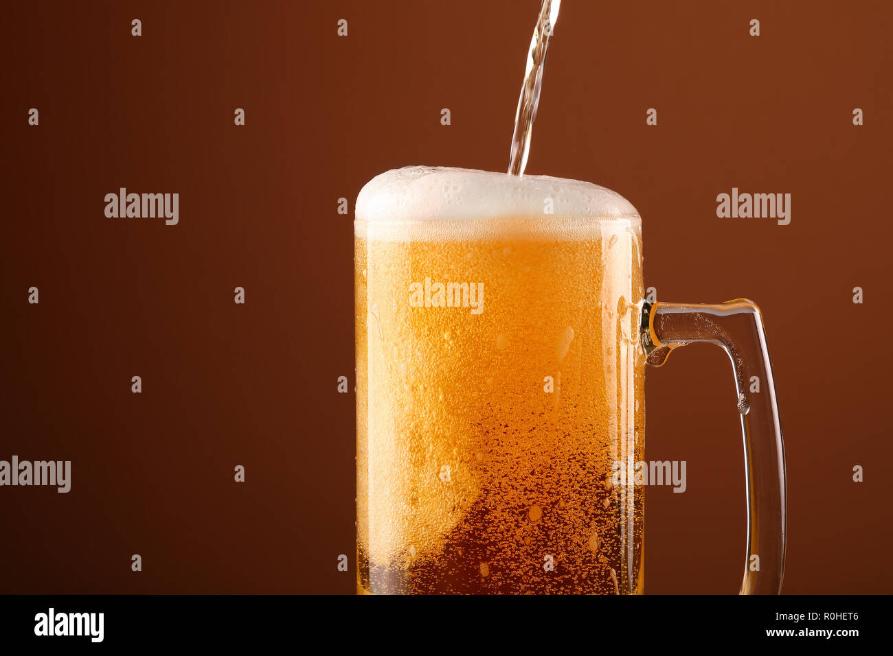 Close up pouring lager beer with white froth and bubbles in glass mug ...