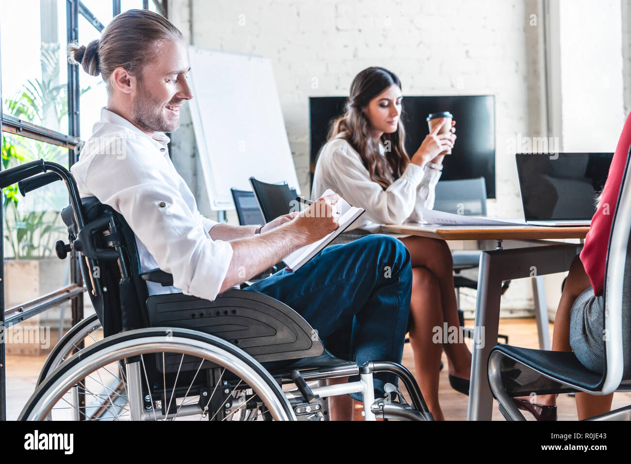 smiling handicapped businessman in wheelchair taking notes at workplace ...