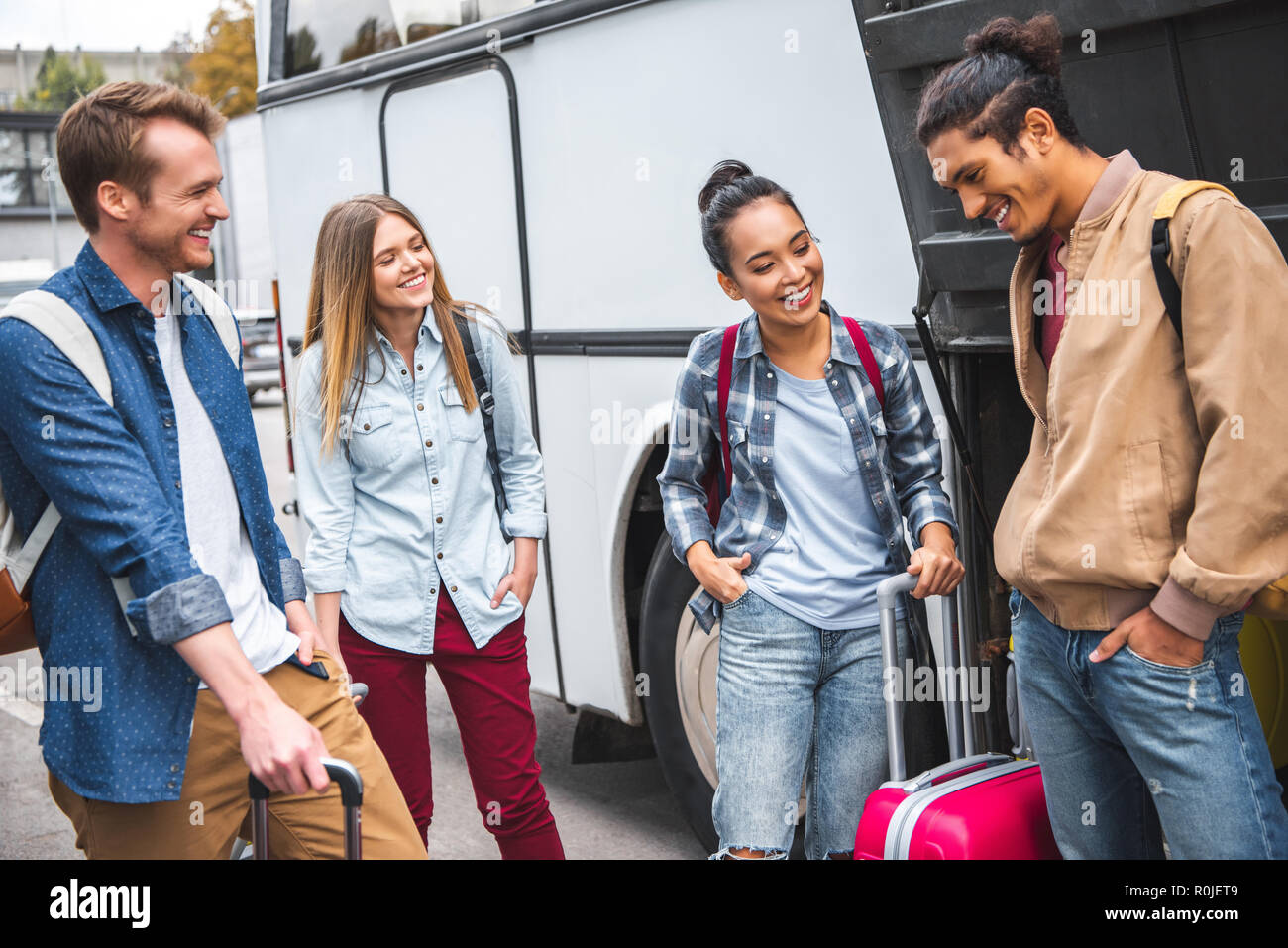 laughing multiethnic tourists with travel bags posing near bus at ...