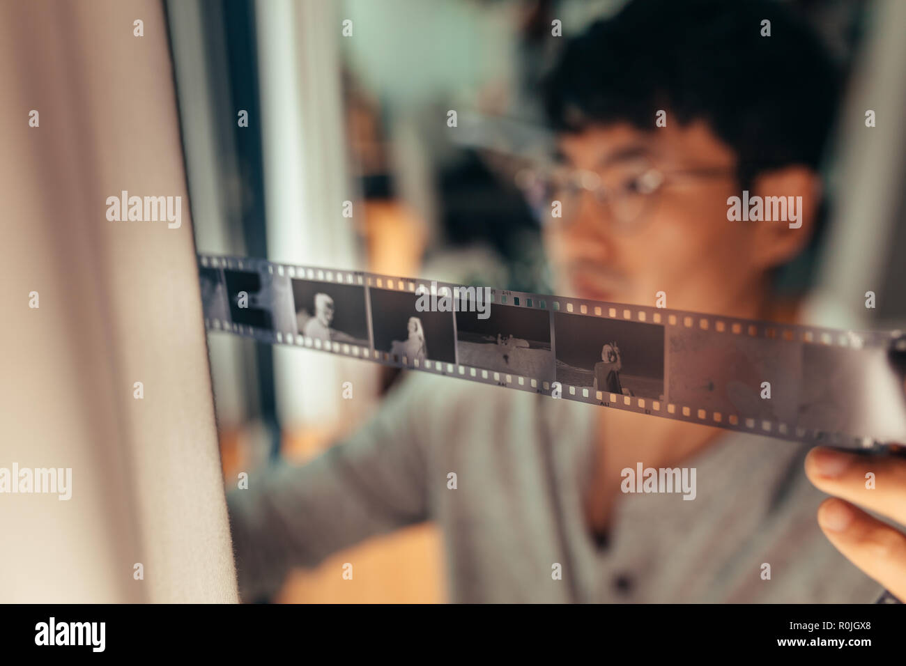 Man checking 35mm filmstrip in front of window. Photographer looking at ...