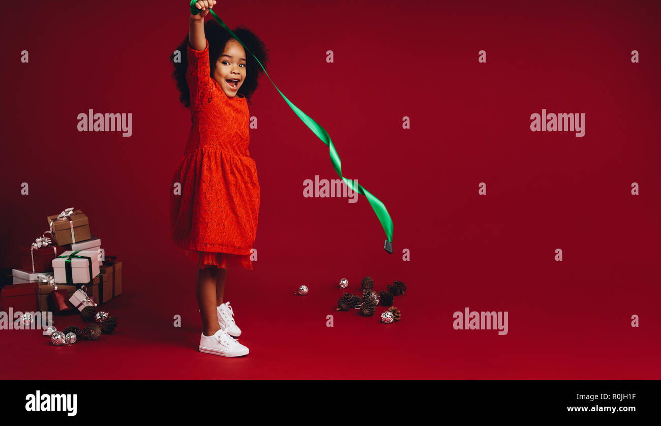 Little girl playing with a ribbon standing beside a pile of gift boxes ...