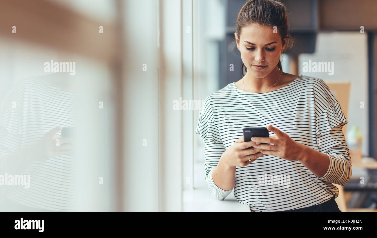Working woman standing beside a window holding mobile phone. Woman ...