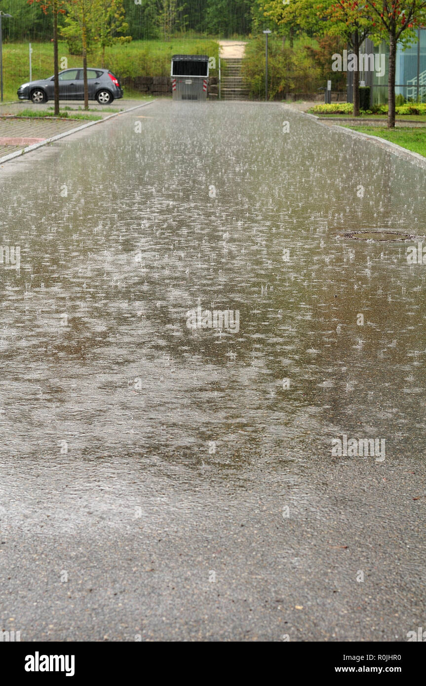 rain in late summer on asphalt road beside office building with parking ...
