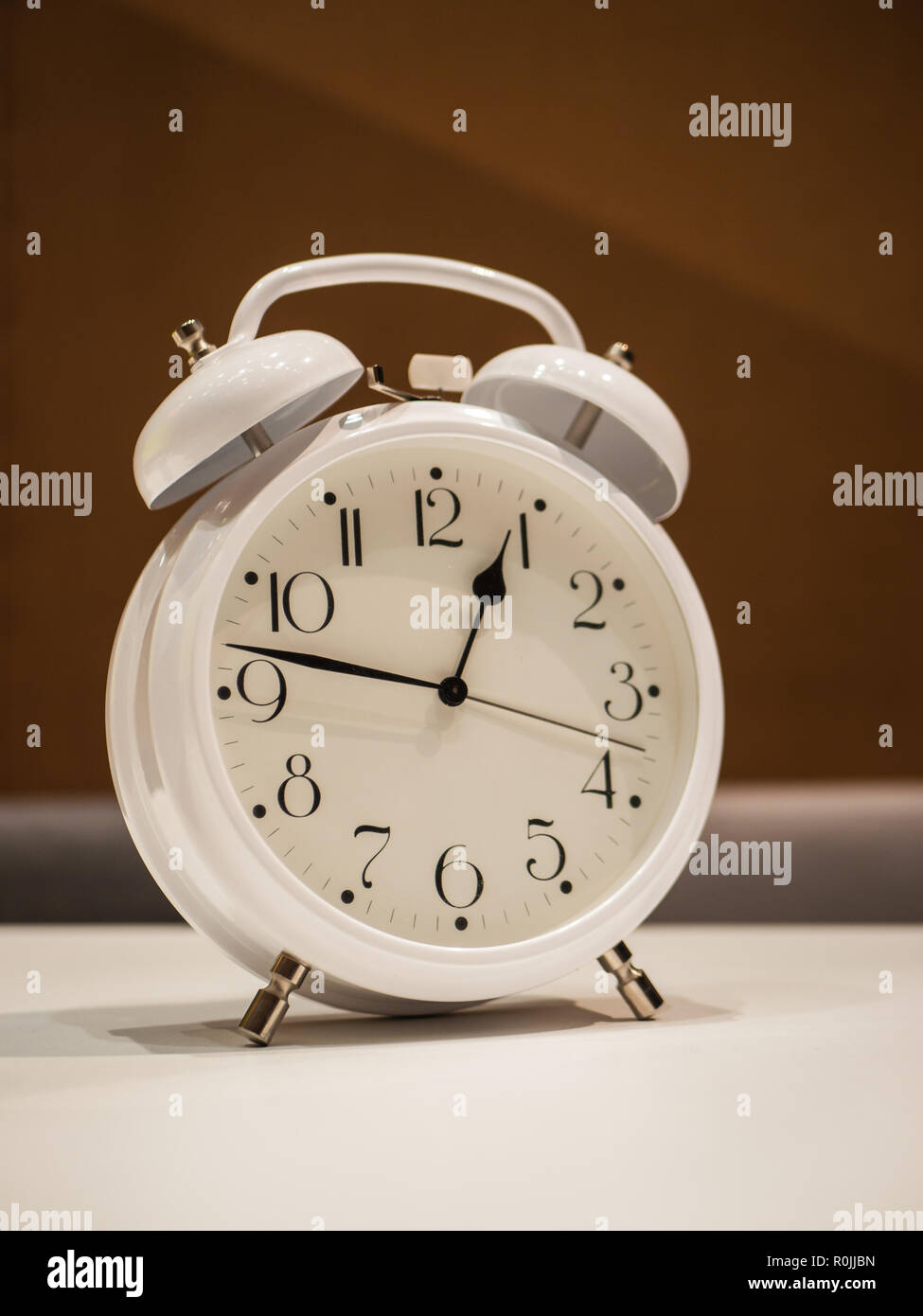 Vintage Alarm Clock standing on a white desk with brown blurry sofa in ...