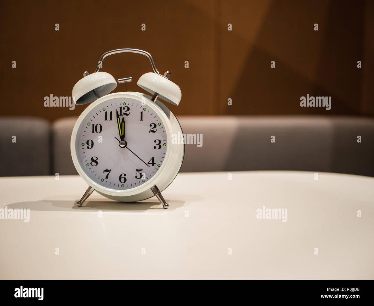 Vintage Alarm Clock standing on a white desk with brown blurry sofa in ...