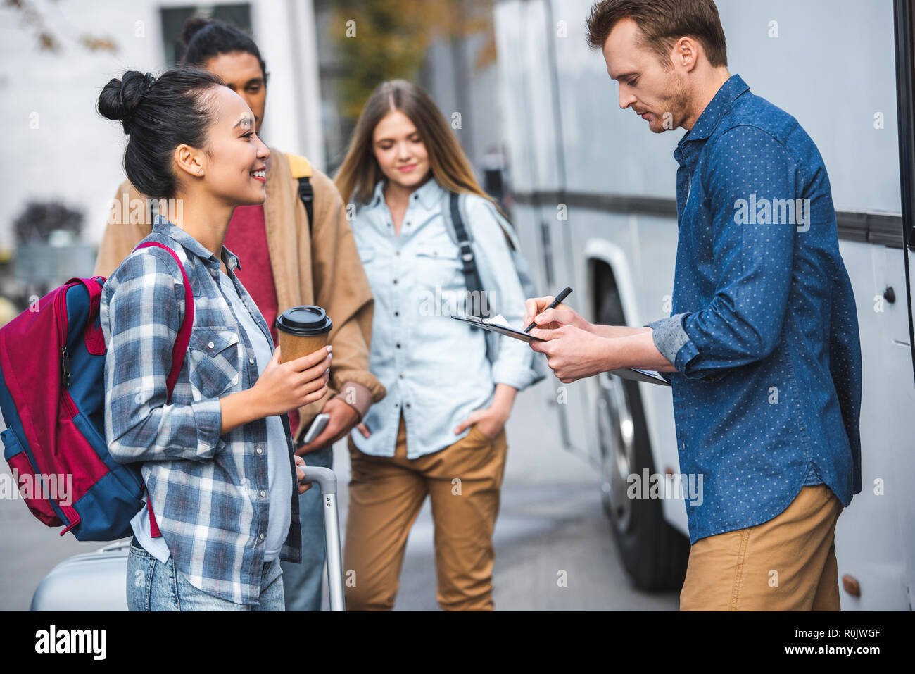 side view of male travel bus controller writing in clipboard while ...