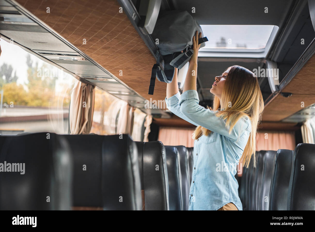 side view of young woman putting backpack on shelf in travel bus Stock ...
