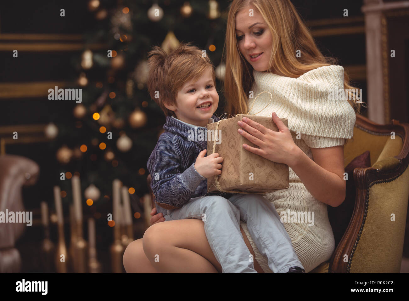 The boy is sitting on his mother's lap with a Christmas present ...