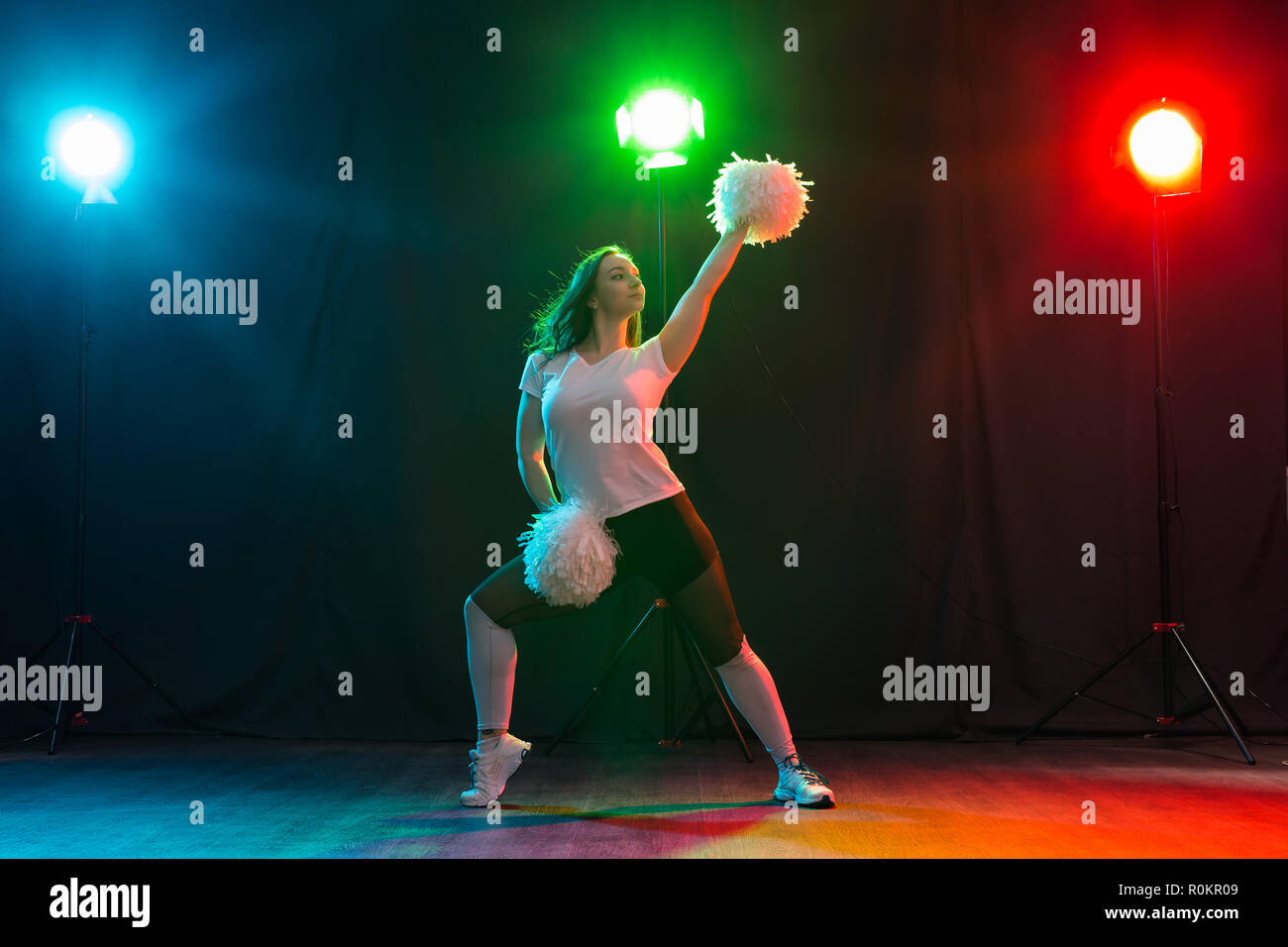 Cheerleading young woman dancing with pom-poms on colourful background ...