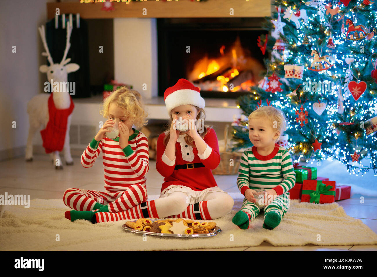 Children at Christmas tree and fireplace drink hot chocolate and eat ...