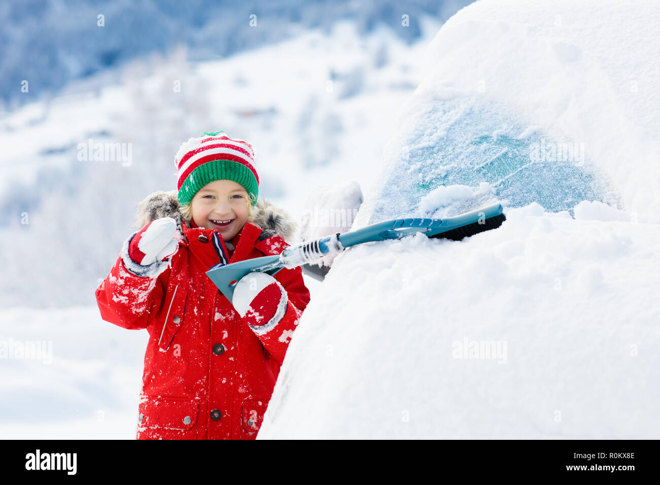 Child brushing snow off car after storm. Kid with winter brush and ...