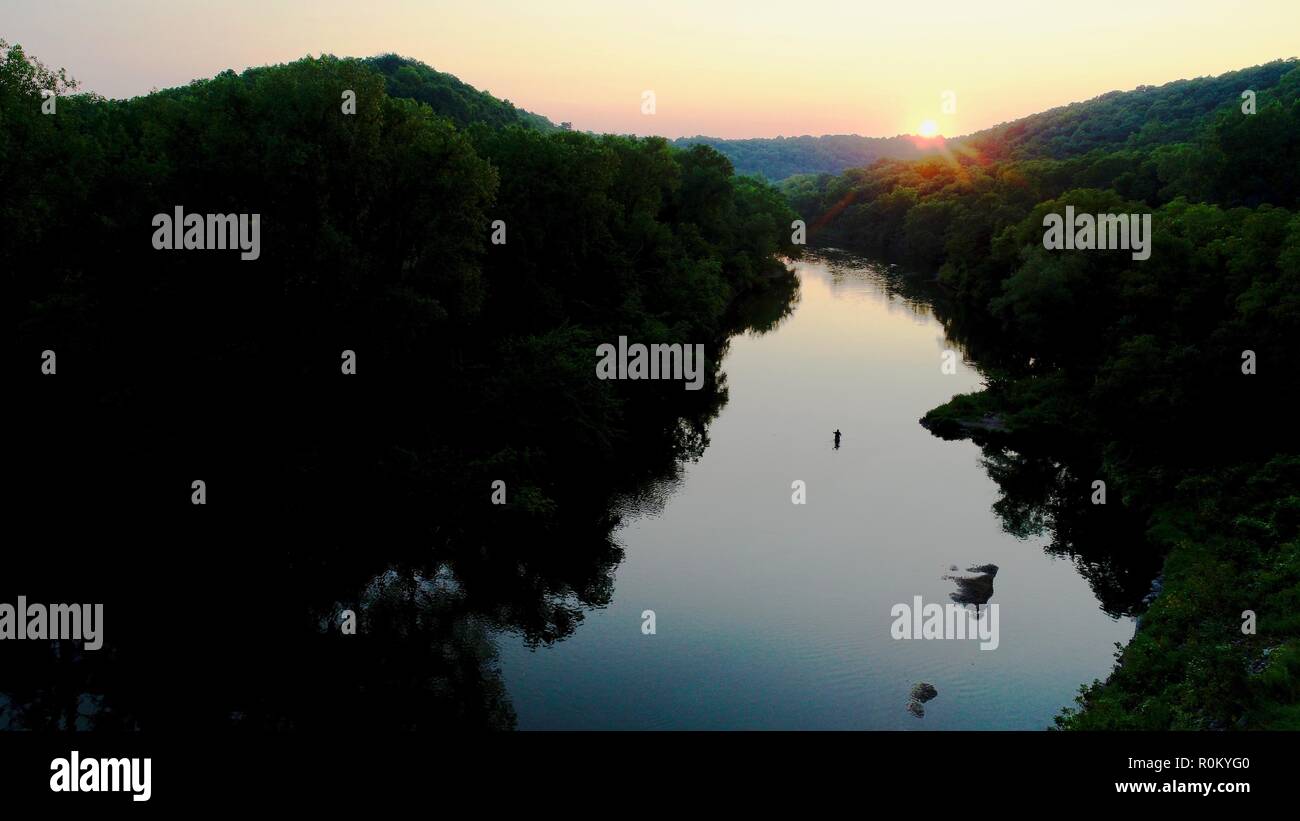 Aerial view of fisherman wading into calm Zumbro River at sunset, with ...