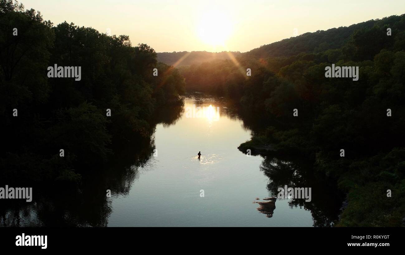 Aerial view of fisherman wading into calm Zumbro River at sunset, with ...