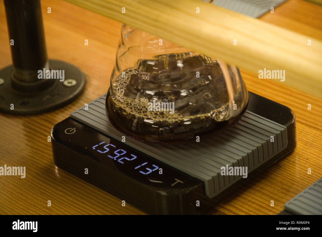 A half-full pot of coffee sits on a scale. There are wooden elements in ...