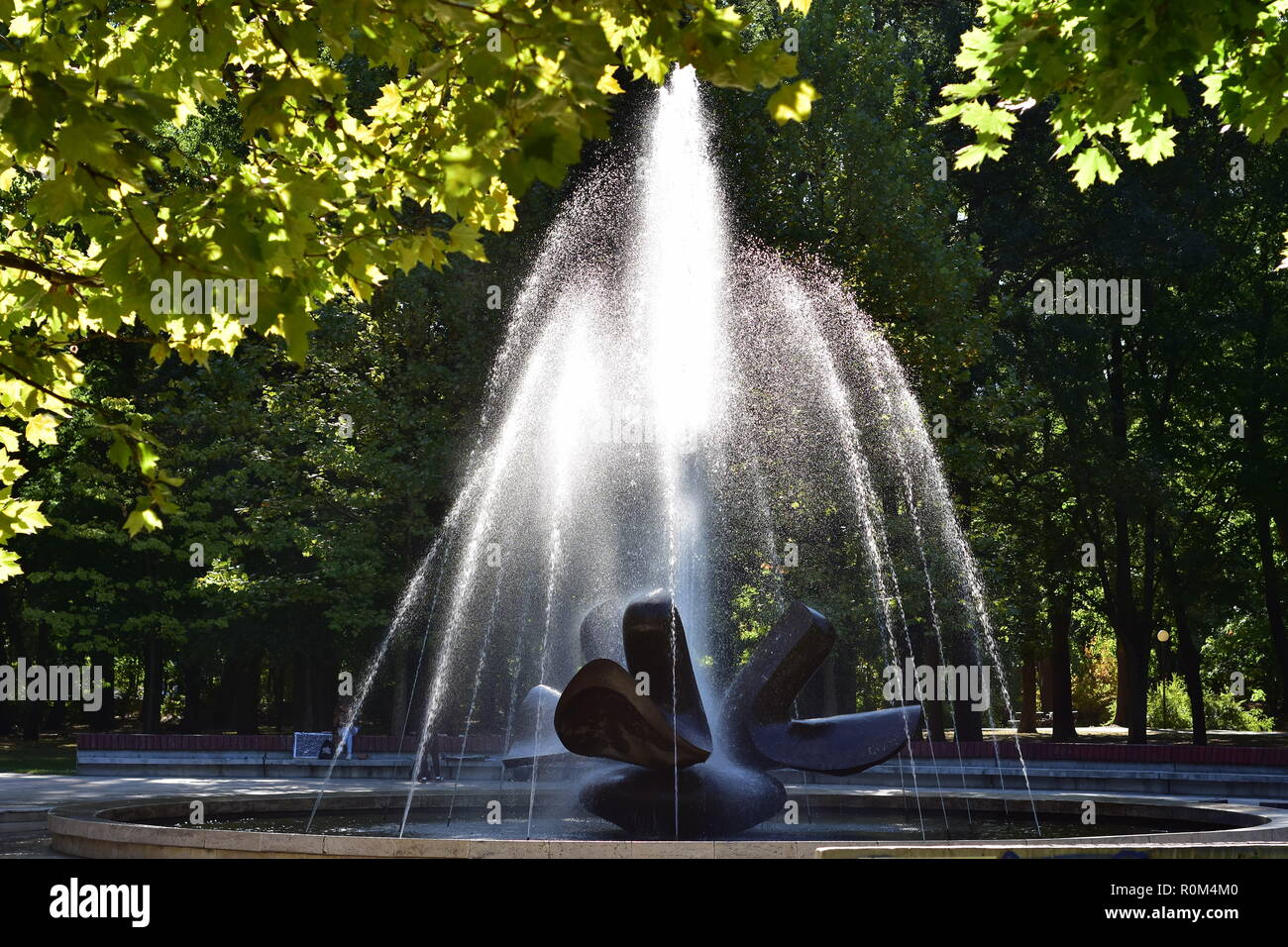 Fountain with bright sunlight reflecting on water drops and spray among ...