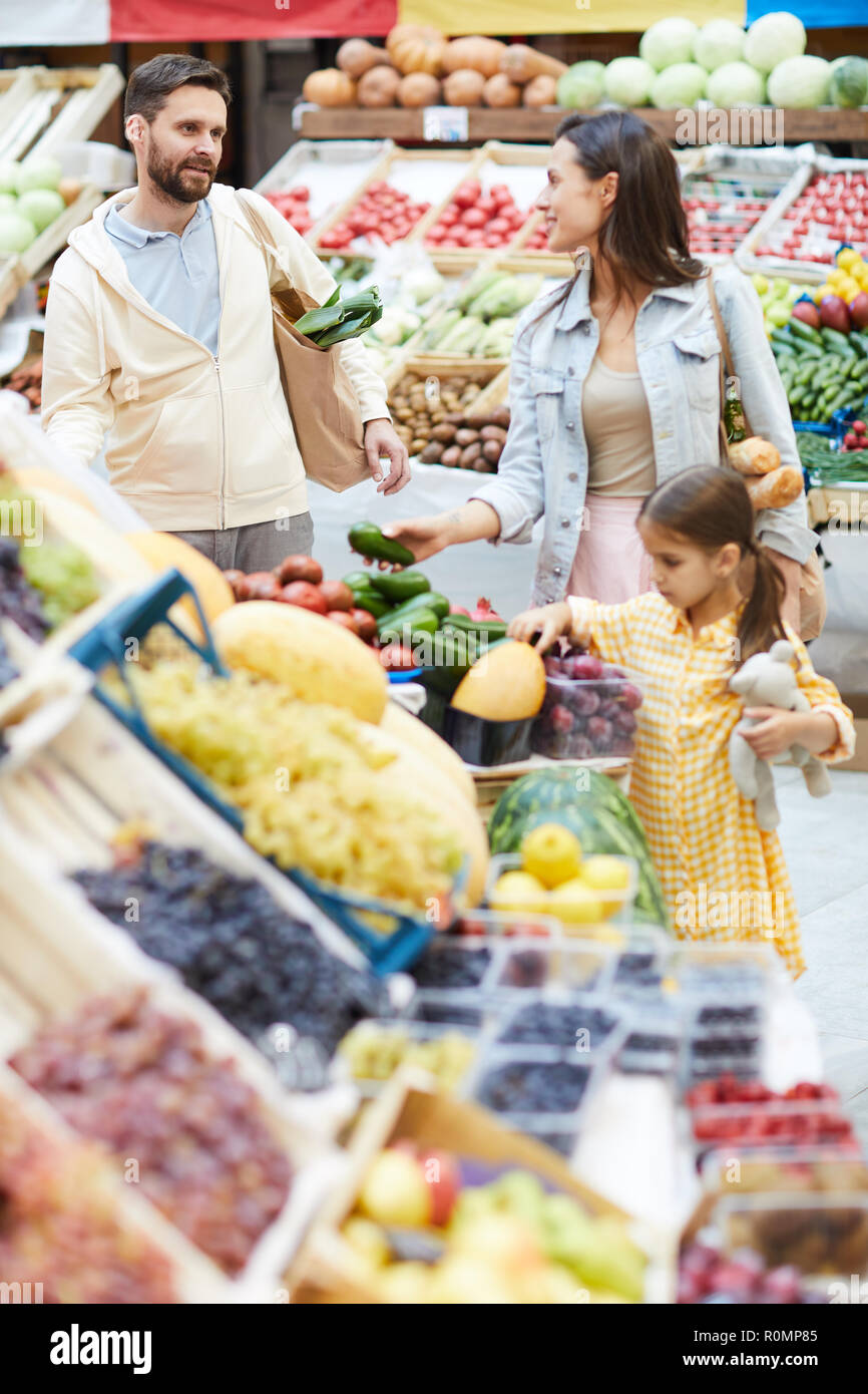 Positive beautiful young family choosing fresh fruits and vegetables ...