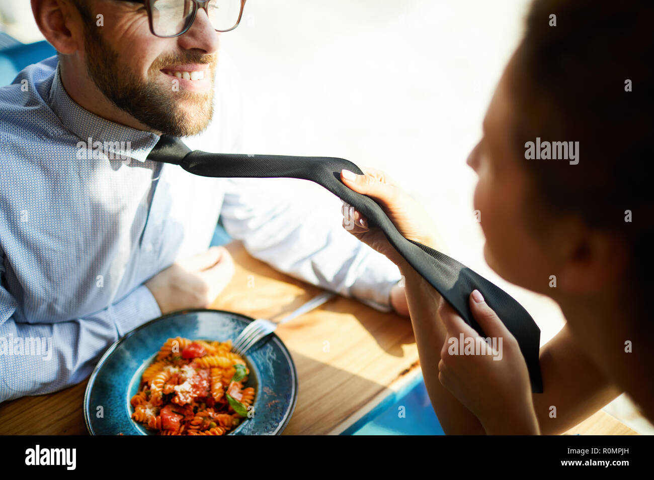Flirty woman pulling smiling man by his tie over served table during ...
