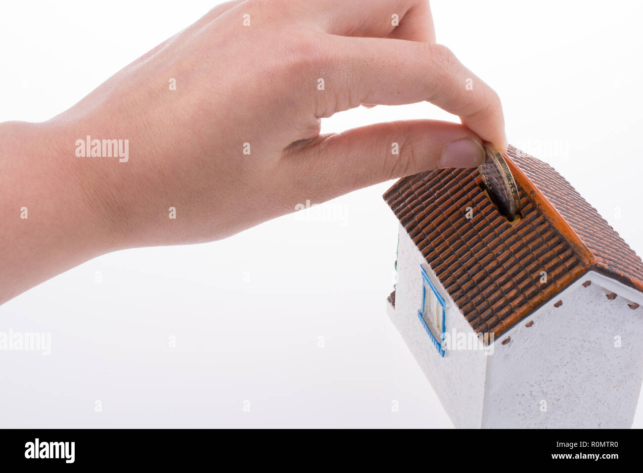 Hand dropping coin into the moneybox in the shape of a model house ...