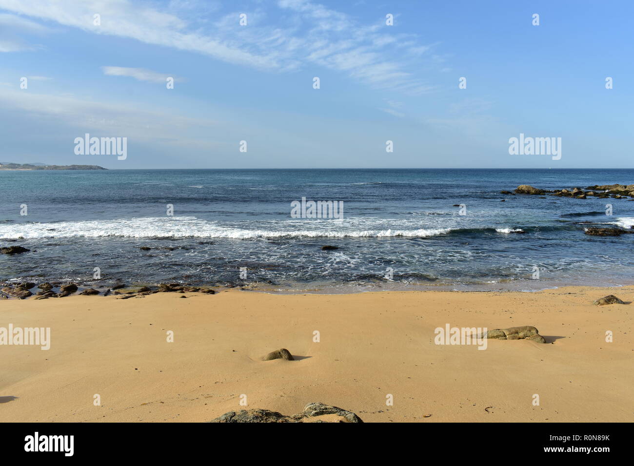 Beach with golden sand, rocks and blue water with waves and foam ...