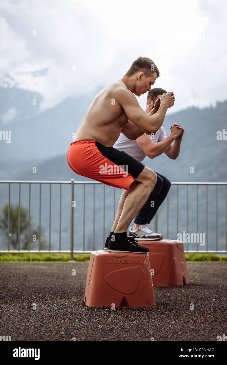 Two male athletic friends doing box jump outdoor on top of the mountain ...
