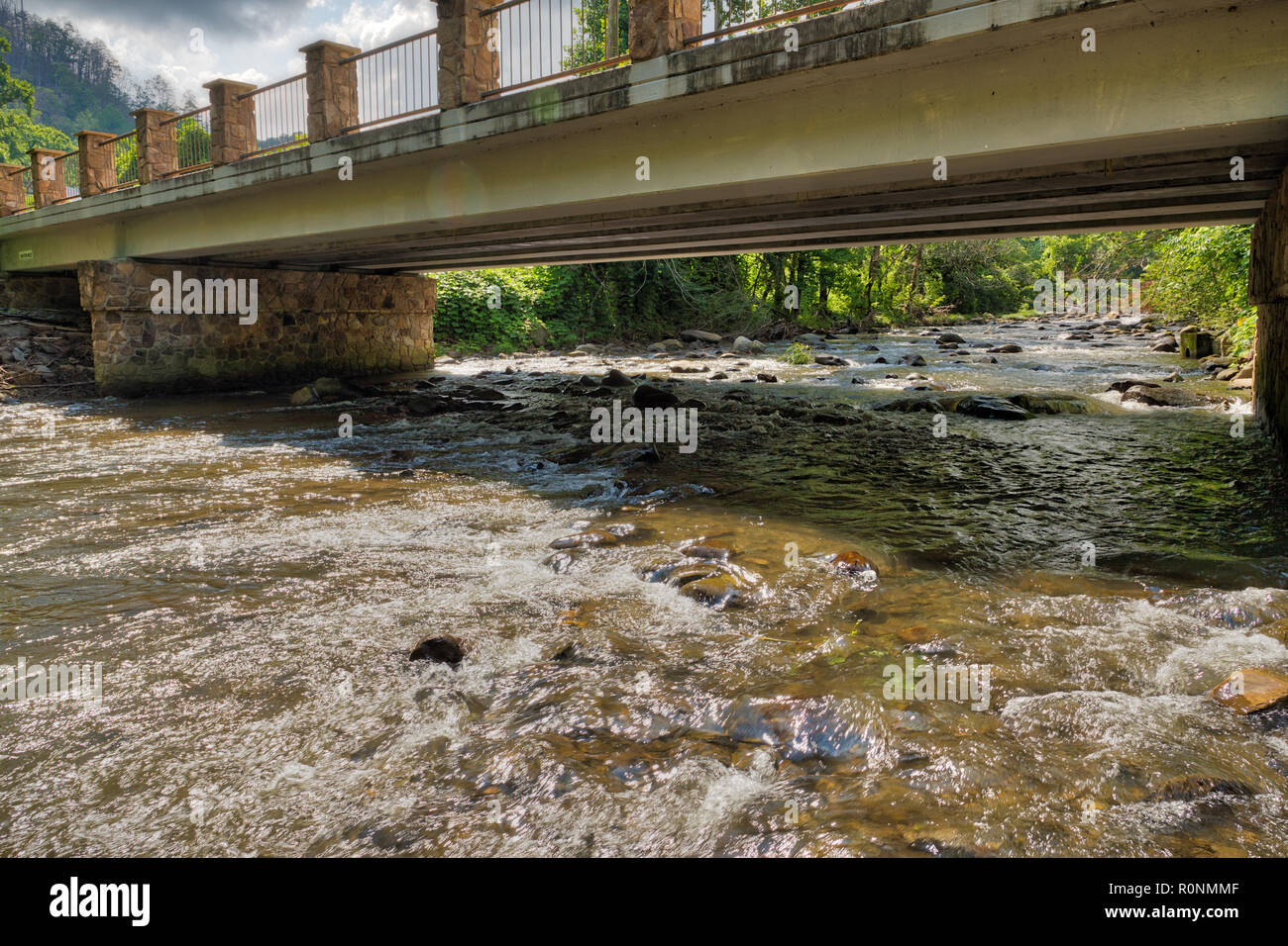 Rapidly flowing river going under a bridge with the sun reflecting ...