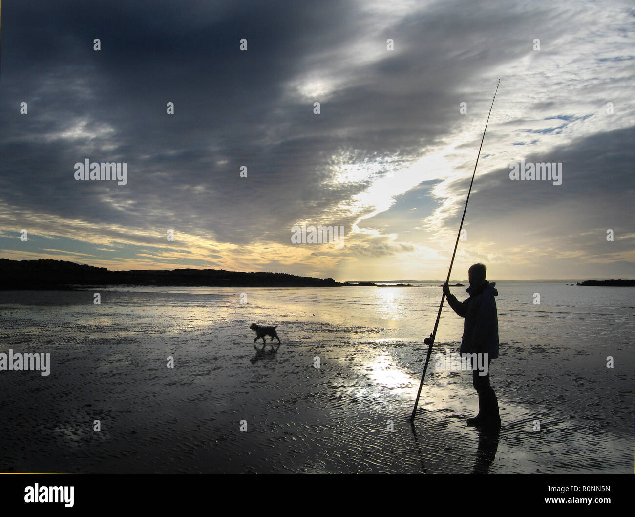 A sea fisherman holds his fishing rod and looks towards the sunset ...