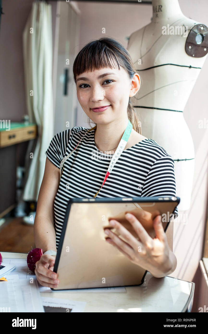 Japanese female fashion designer working in a studio, holding digital ...