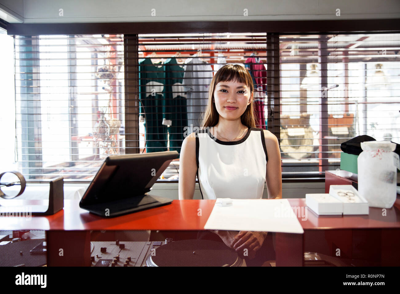 Smiling Japanese saleswoman standing at a counter in clothing store ...