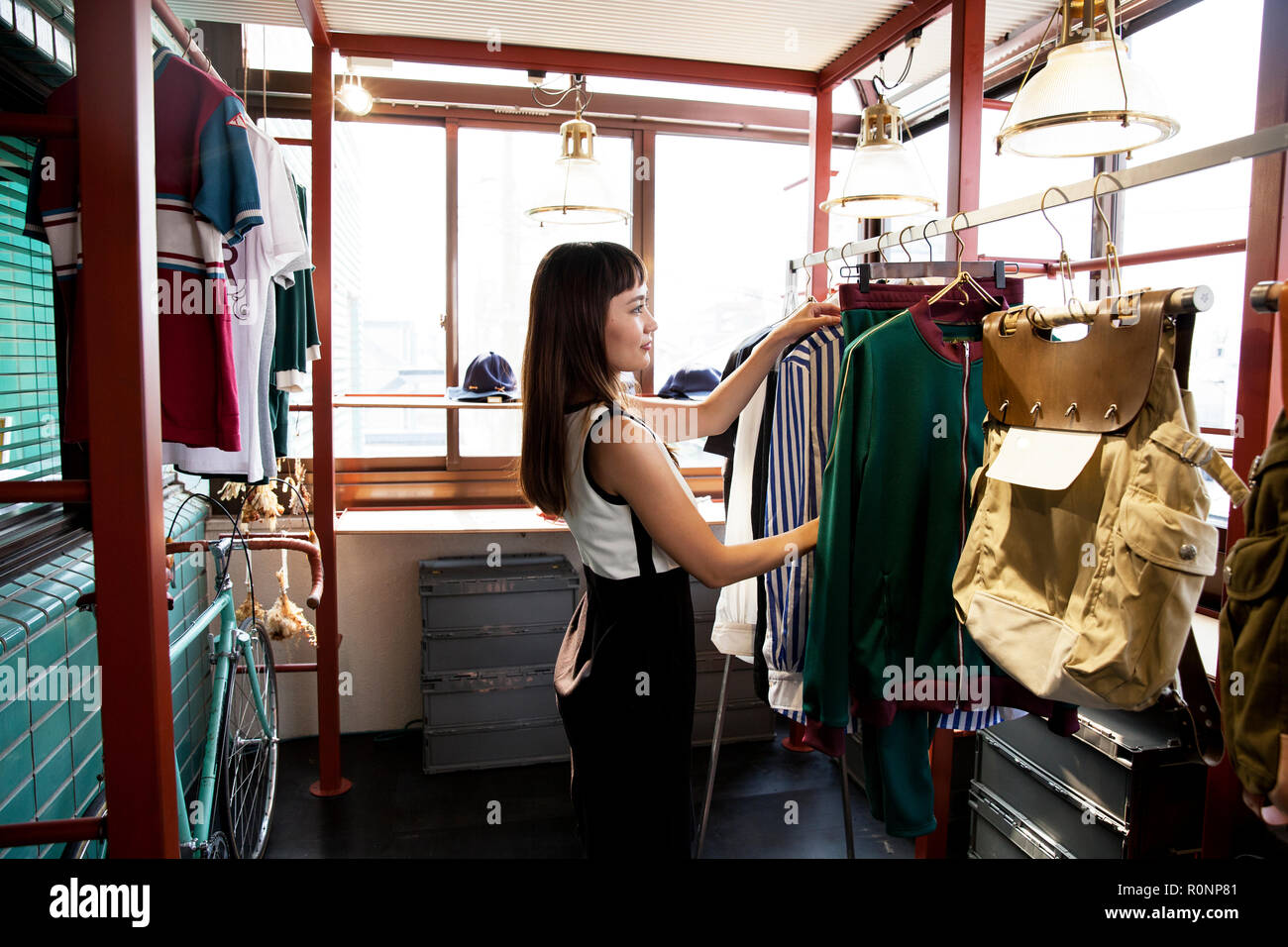Japanese saleswoman standing in clothing store, arranging clothes on a ...