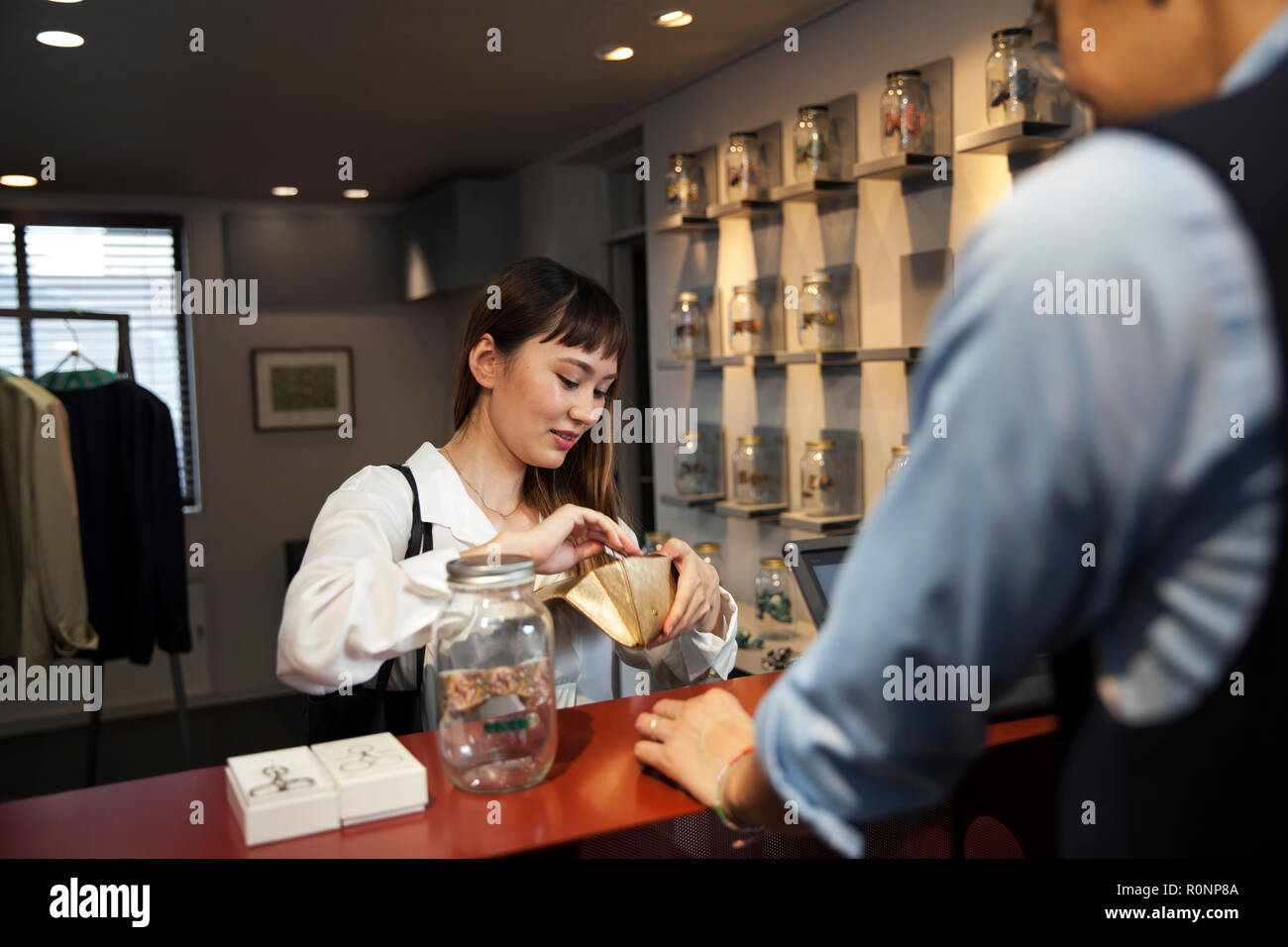 Smiling Japanese woman standing at counter in clothing store, paying ...