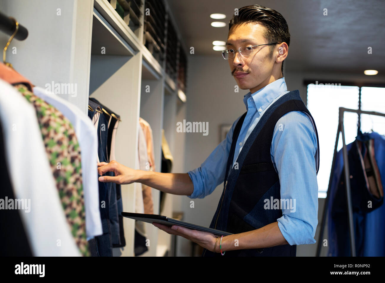 Japanese salesman with moustache wearing glasses standing in clothing ...