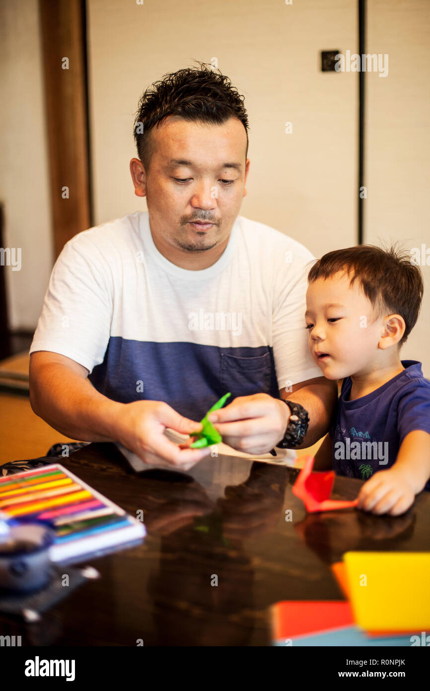 Japanese man and little boy sitting at a table, making Origami animals ...