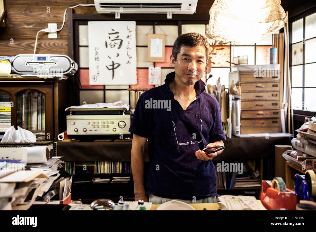 Japanese man standing in a Washi producing workshop holding a smart ...