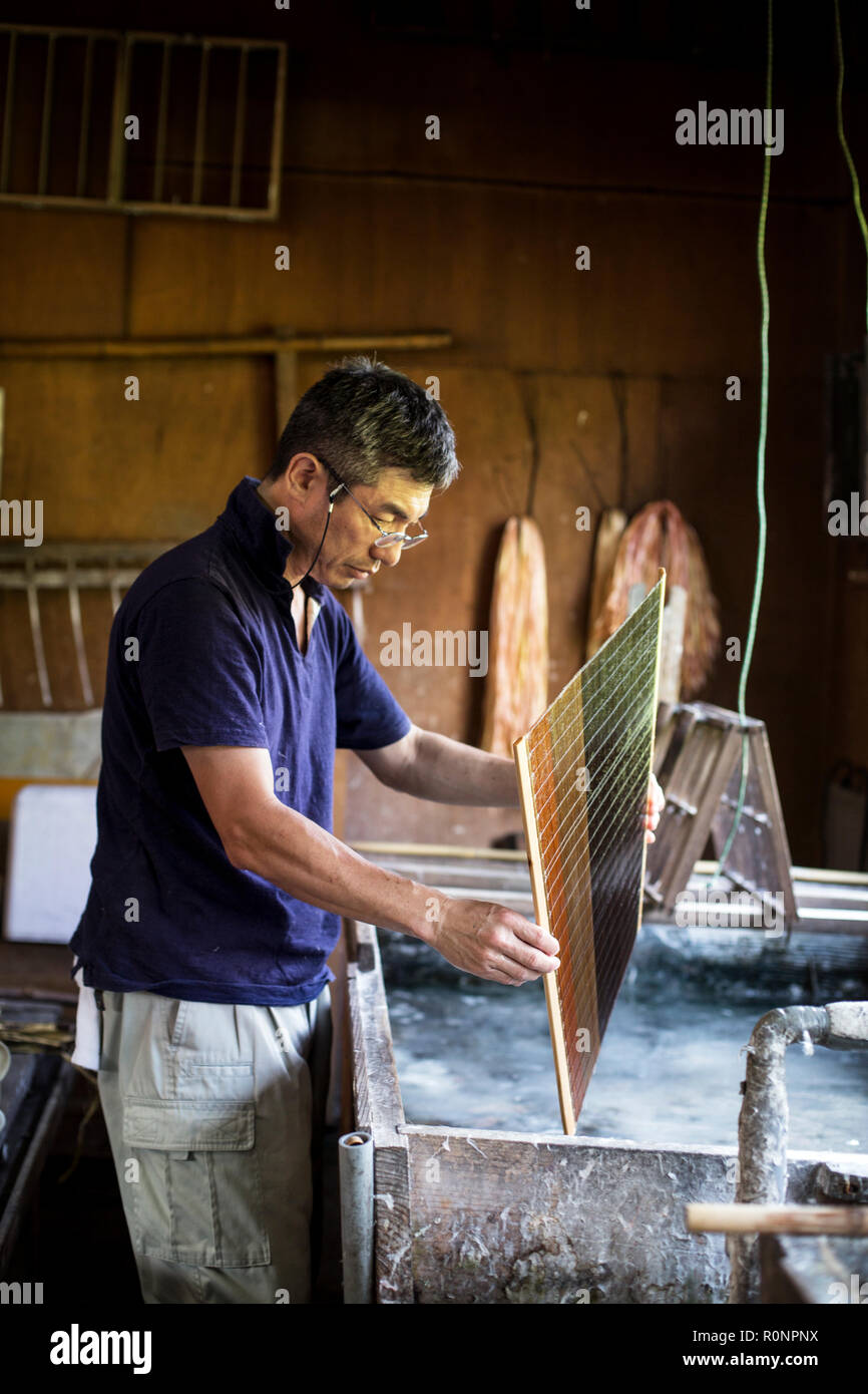 Japanese man in a workshop holding a wooden frame of dried pulp over a ...