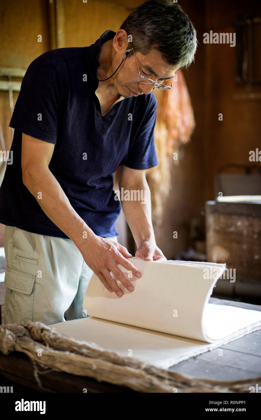 Japanese man standing in a workshop, checking through sheets of ...
