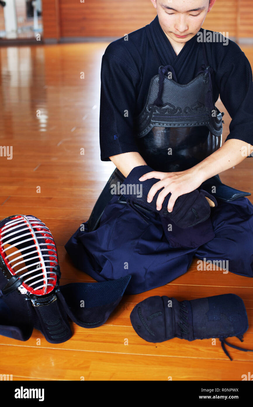 Male Japanese Kendo fighter kneeling on wooden floor, putting on Kote ...
