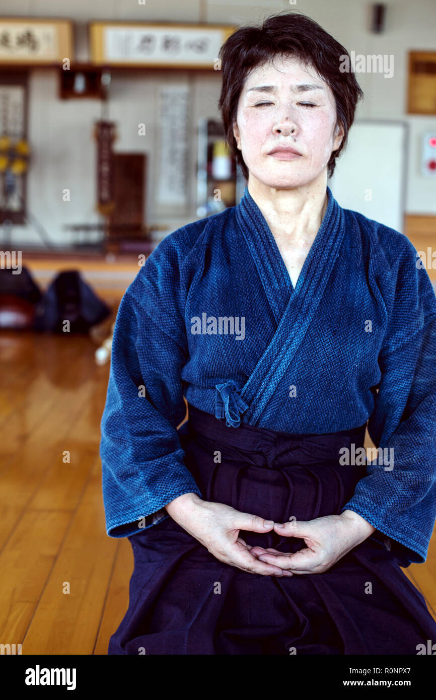 Female Japanese Kendo fighter kneeling on wooden floor, meditating ...