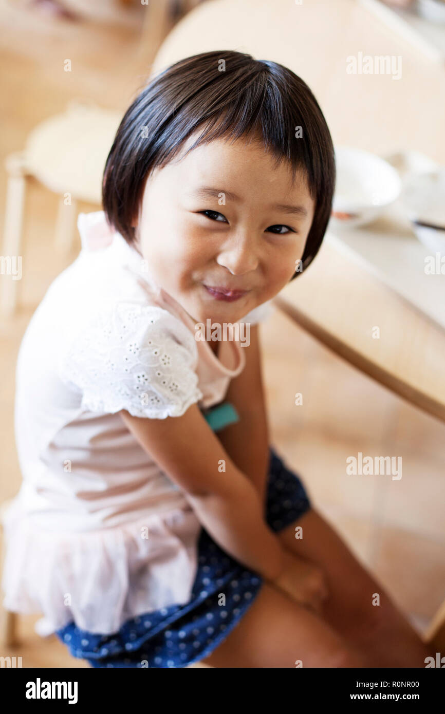 A smiling girl sitting on the floor in a Japanese preschool, looking at ...