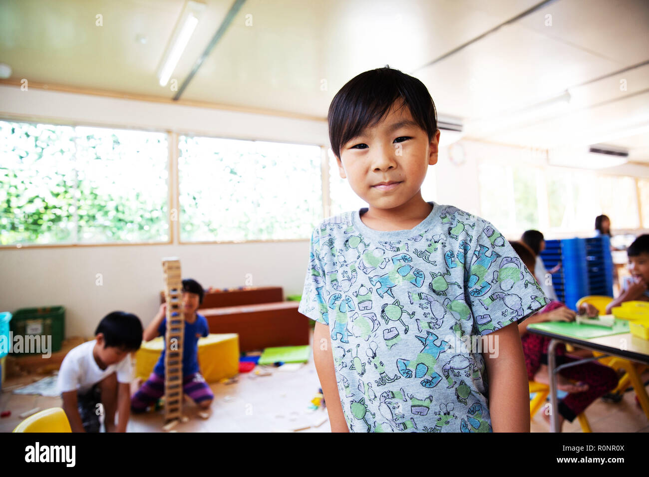 Young boy standing in a classroom in a Japanese preschool, smiling at ...