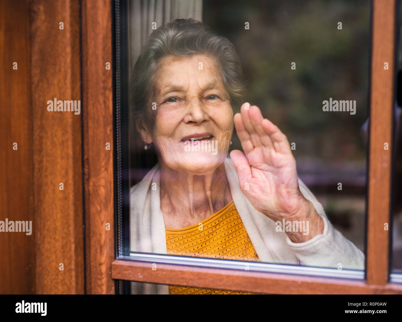 An elderly woman standing by the window, looking out. Shot through ...